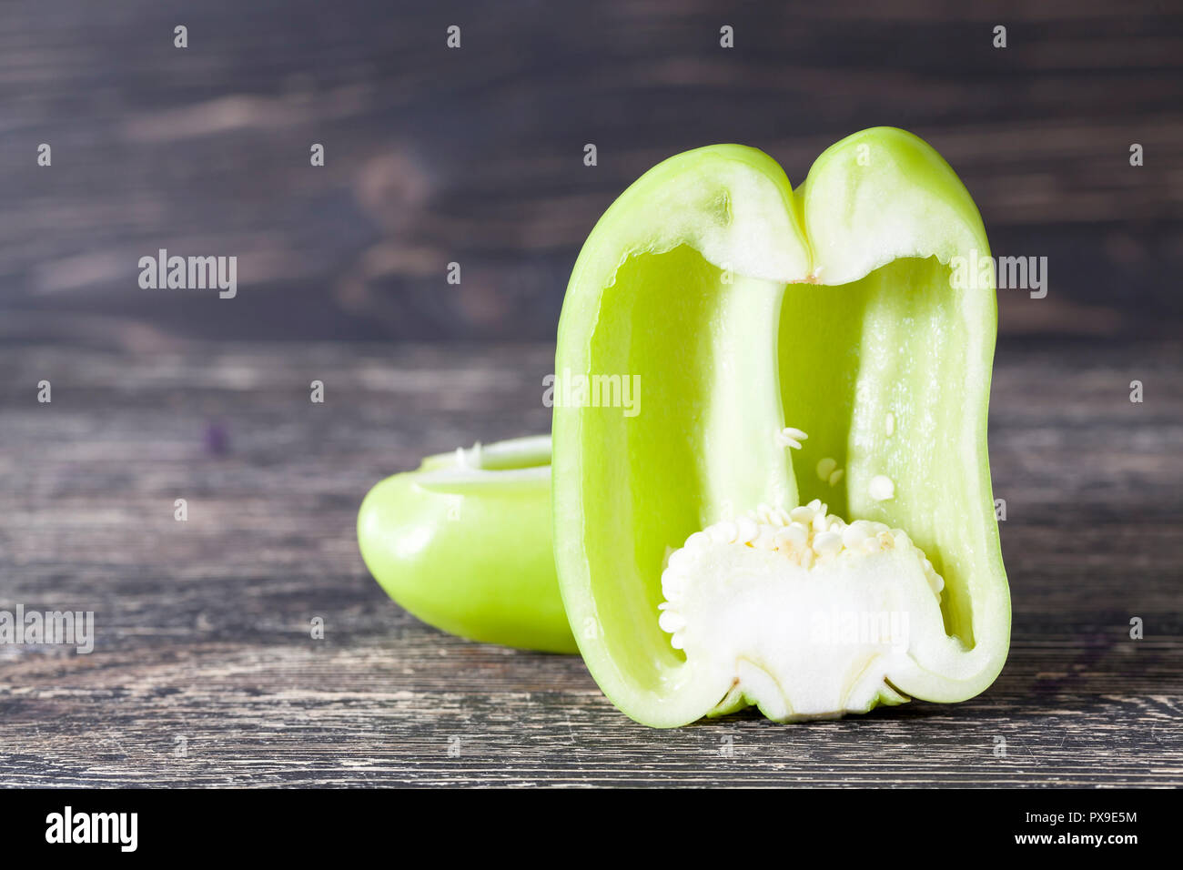 cut into half one pepper green, on a black board with a black wall ...