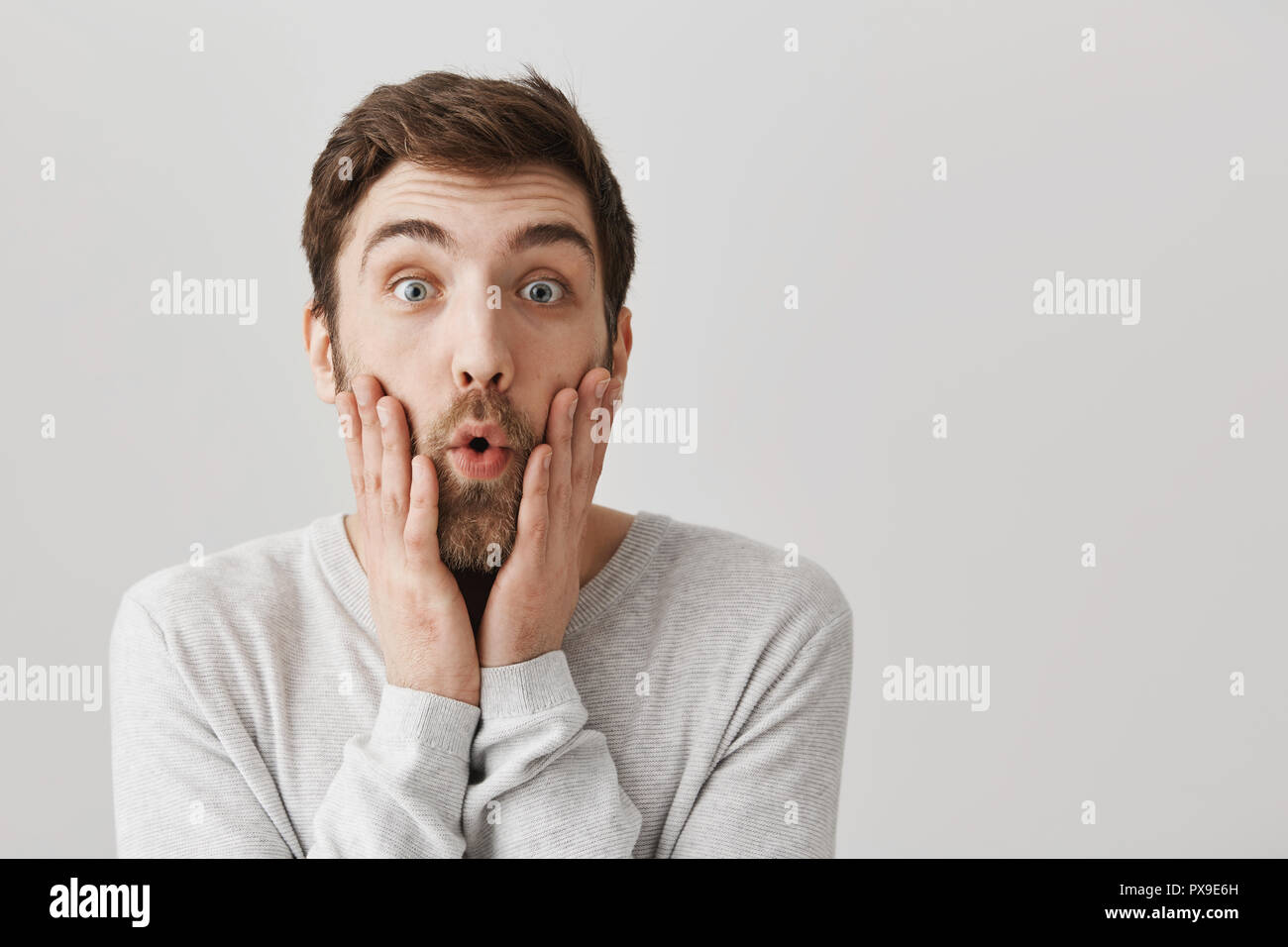 Ordinary slender european male model with beard holding hands on cheeks ...