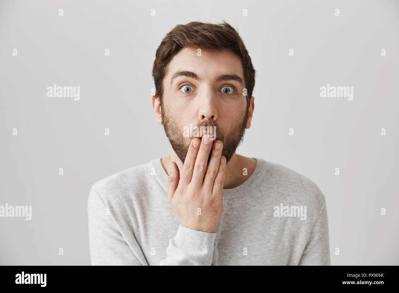 Close-up portrait of amazed and shocked young guy with beard, covering ...