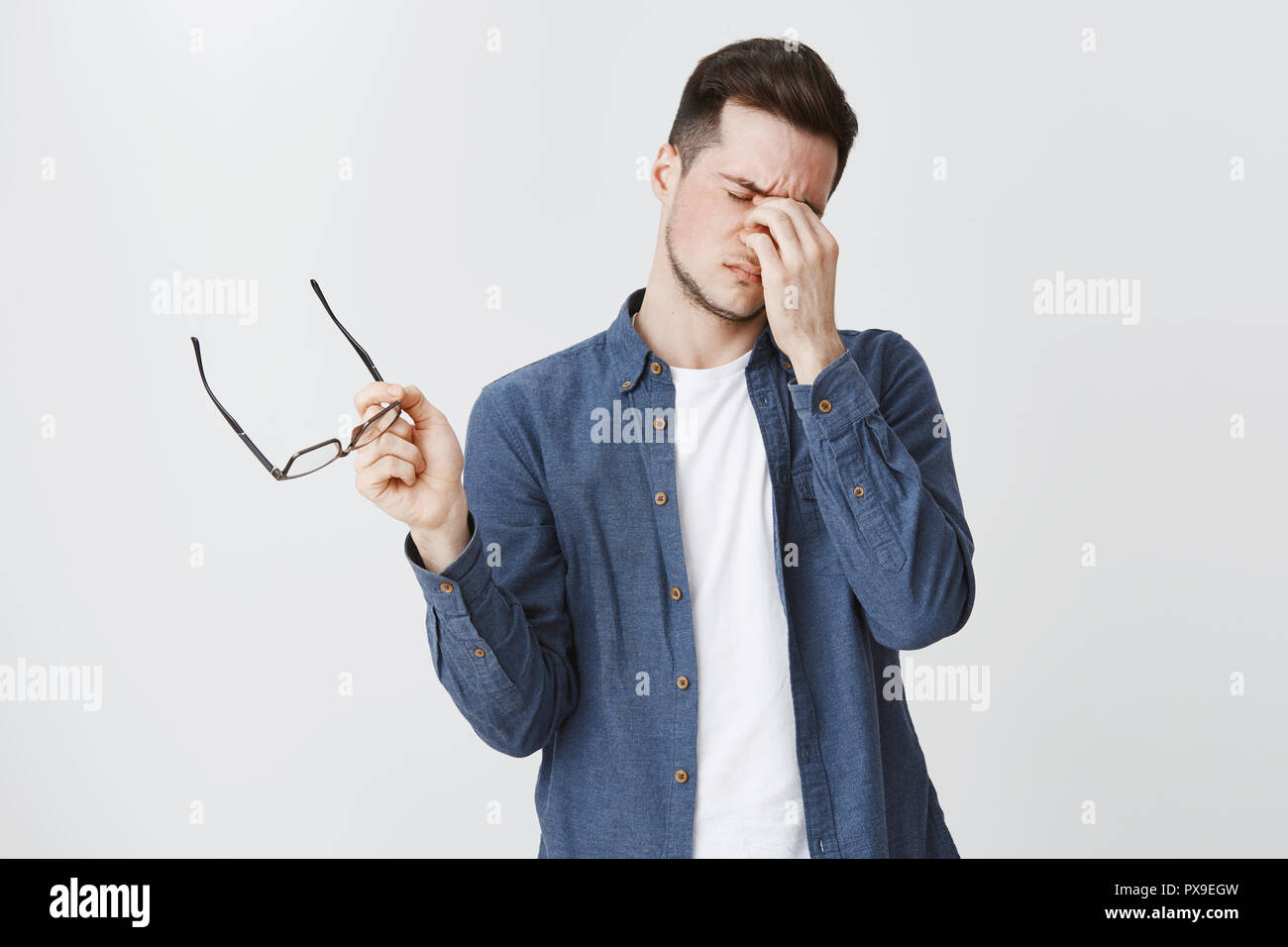Guy rubbing eyes as feeling tired after wearing glasses while working ...