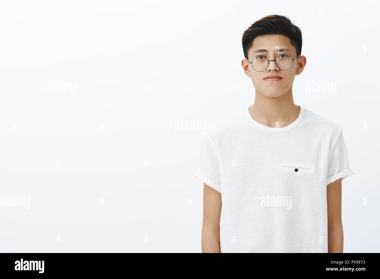 Charming young chinese guy in trendy glasses and t-shirt standing to ...