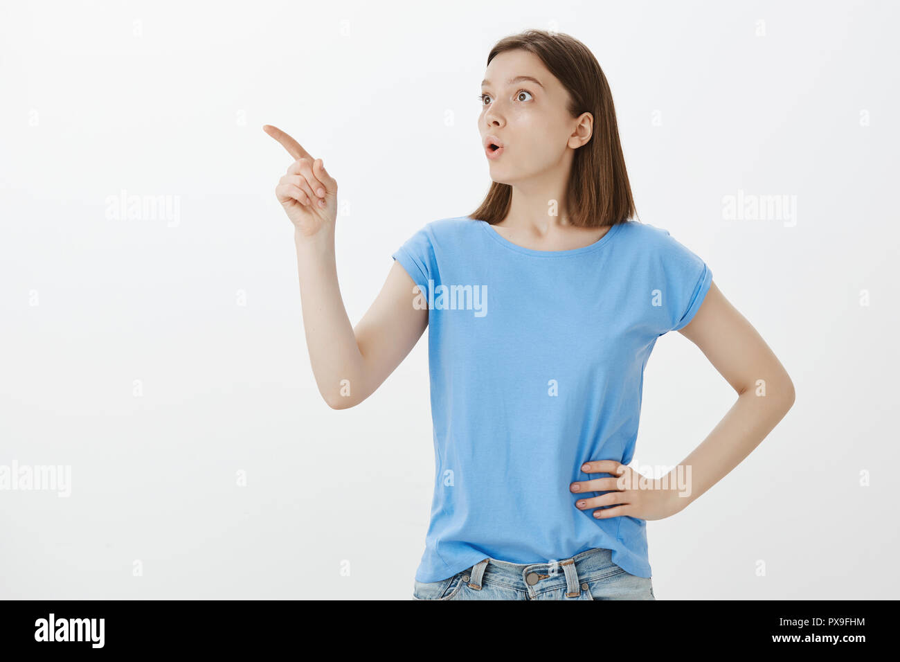 Impressed good-looking girl in blue t-shirt, holding hand on hip ...