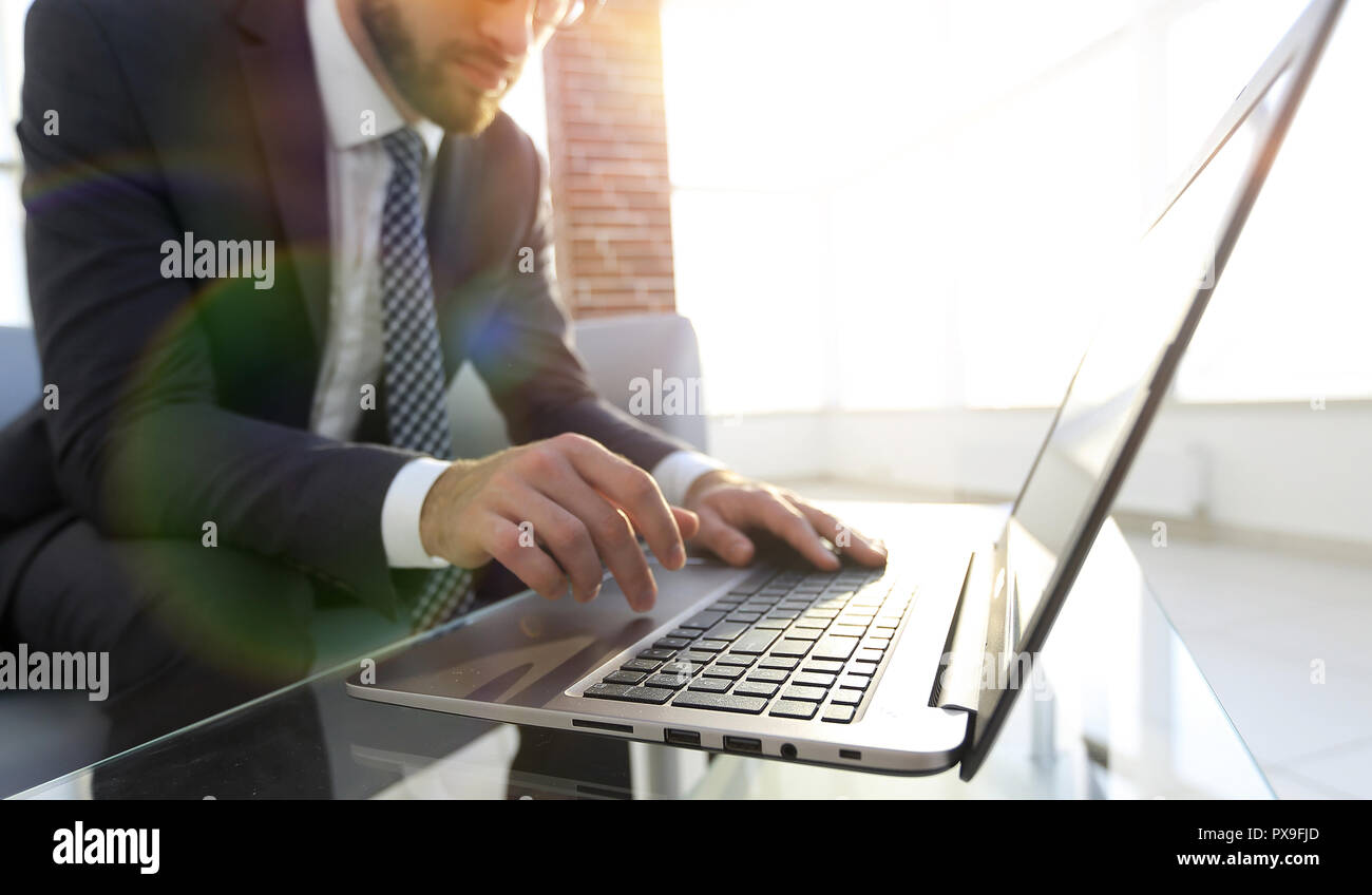 Concentrated young businessman is typing information on his laptop at ...