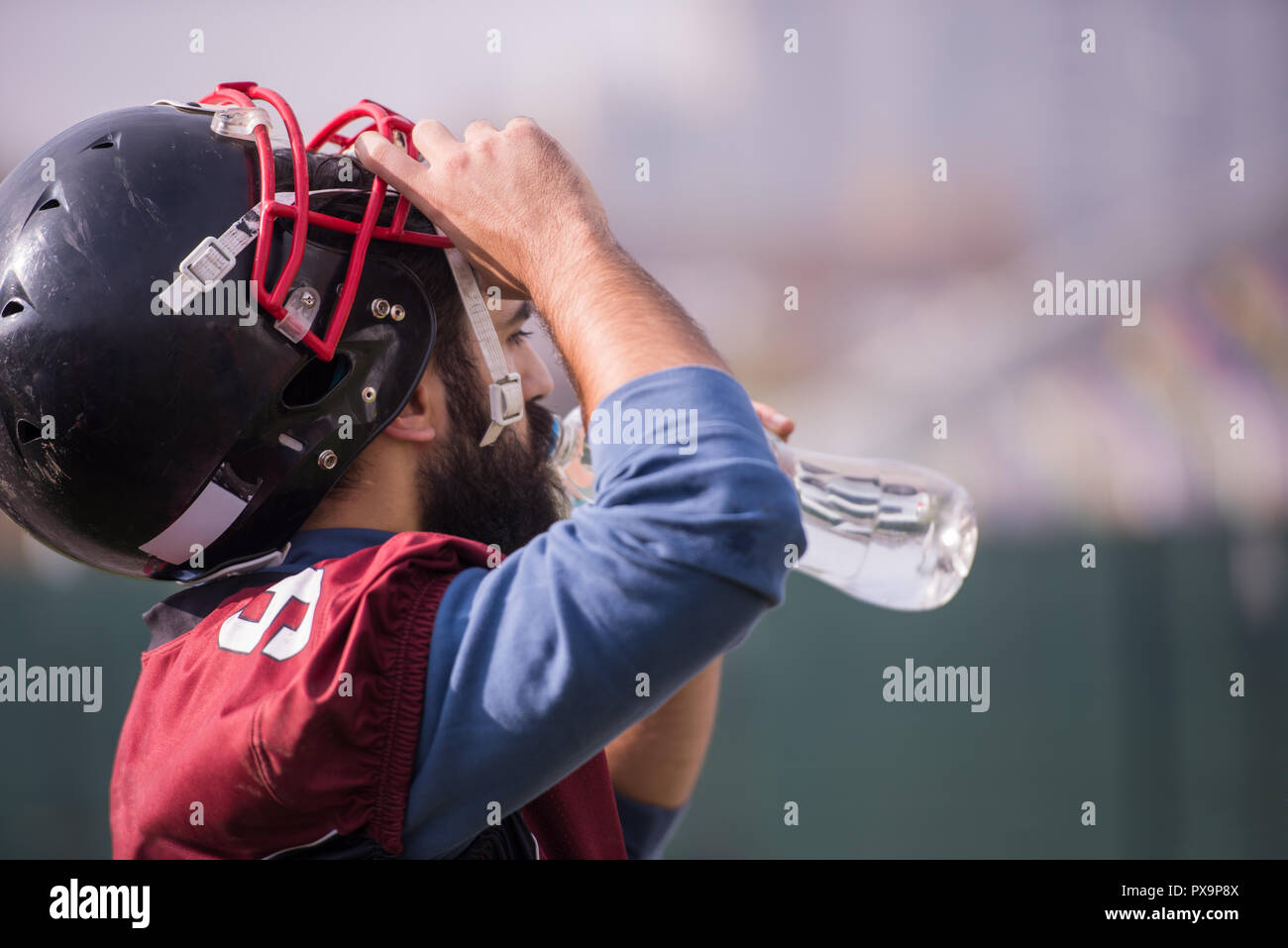 A tired american football player drinking water while resting after ...