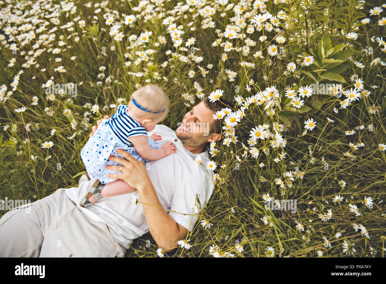 A little baby girl and his father enjoying outdoors in field of daisy ...