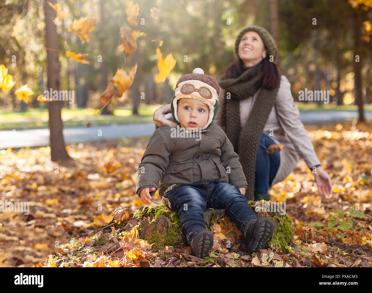 Little boy sitting on a stump near mother with leaflets in the park ...