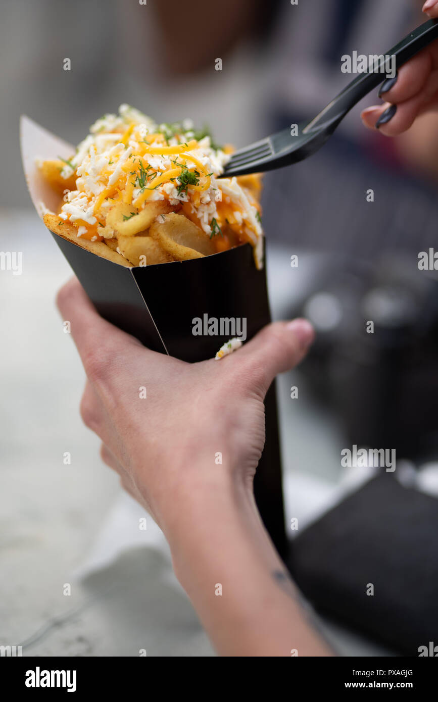 Closeup of hand holding fries with cheddar cheese, white cheee and dip ...