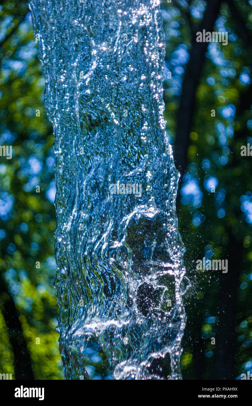 transparent falling water vertical flows against a blue sky and green ...