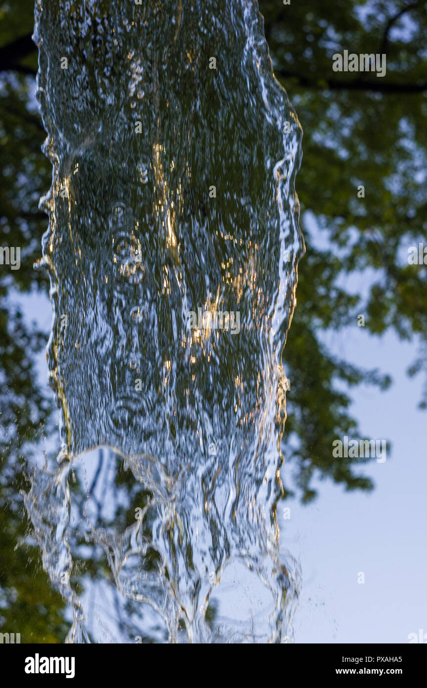 transparent falling water vertical flows against a blue sky and green ...