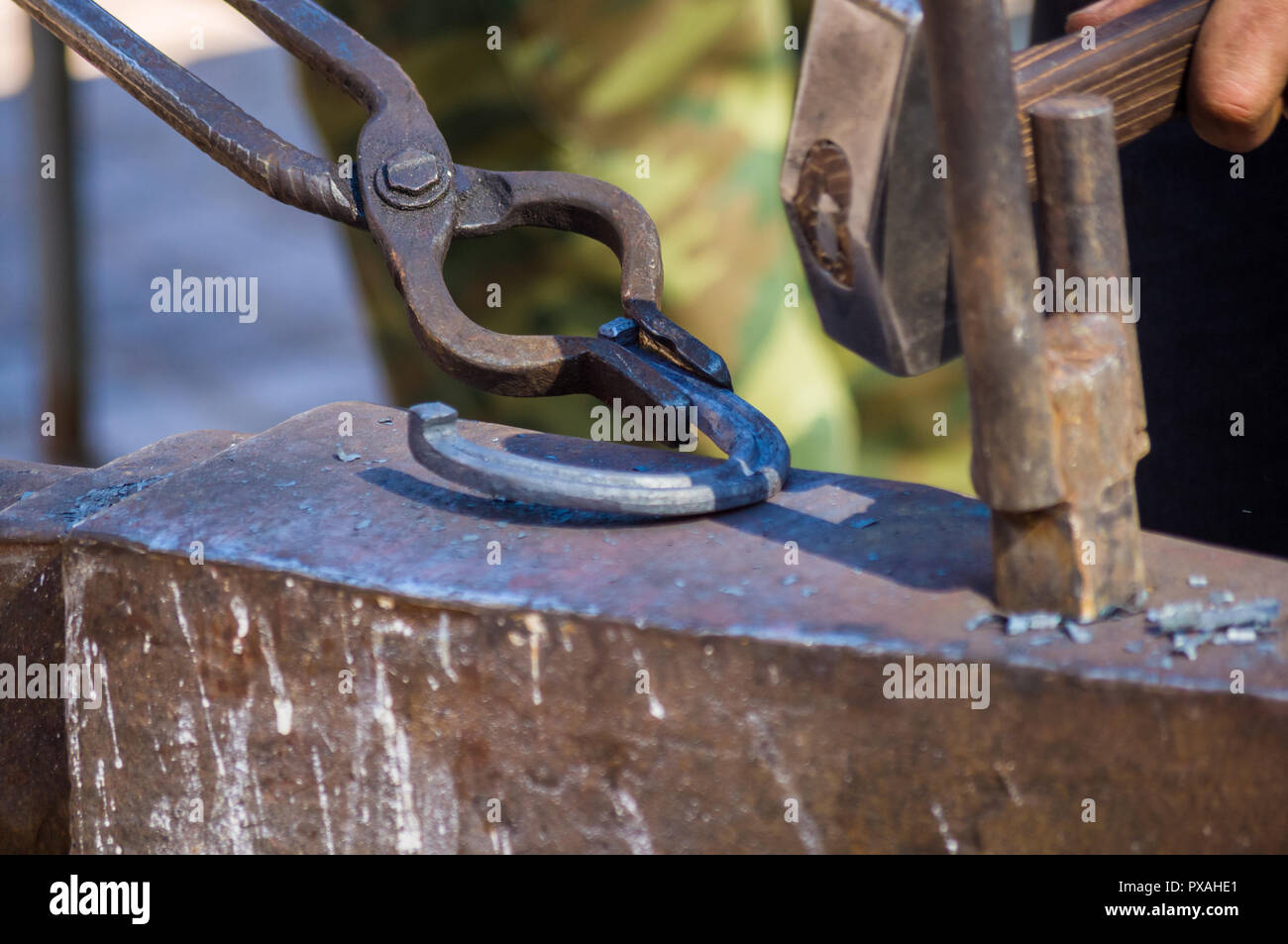 blacksmith performs the forging of hot glowing horseshoe on the anvil ...