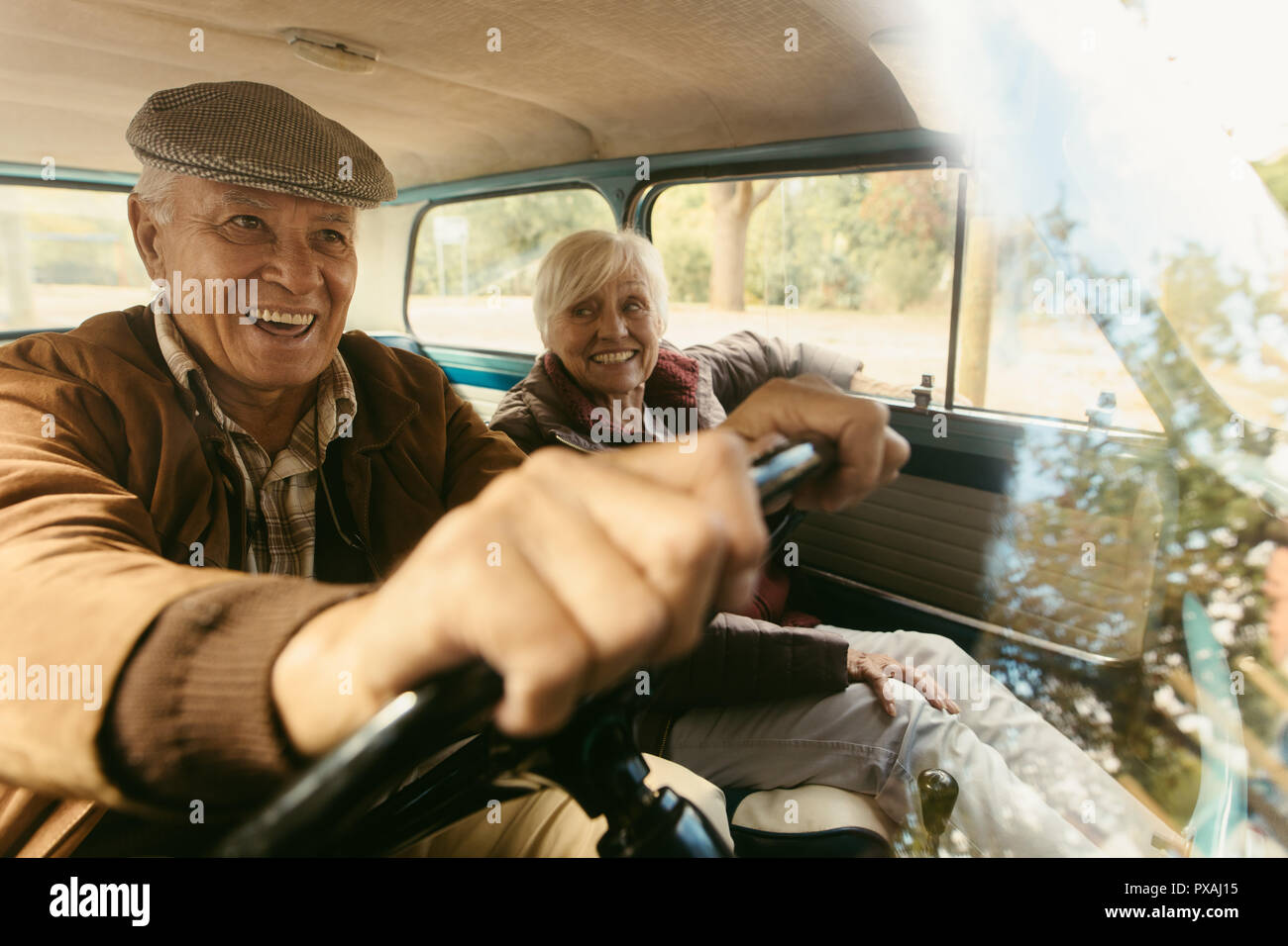 Smiling senior man driving a old car with a woman sitting next to him ...