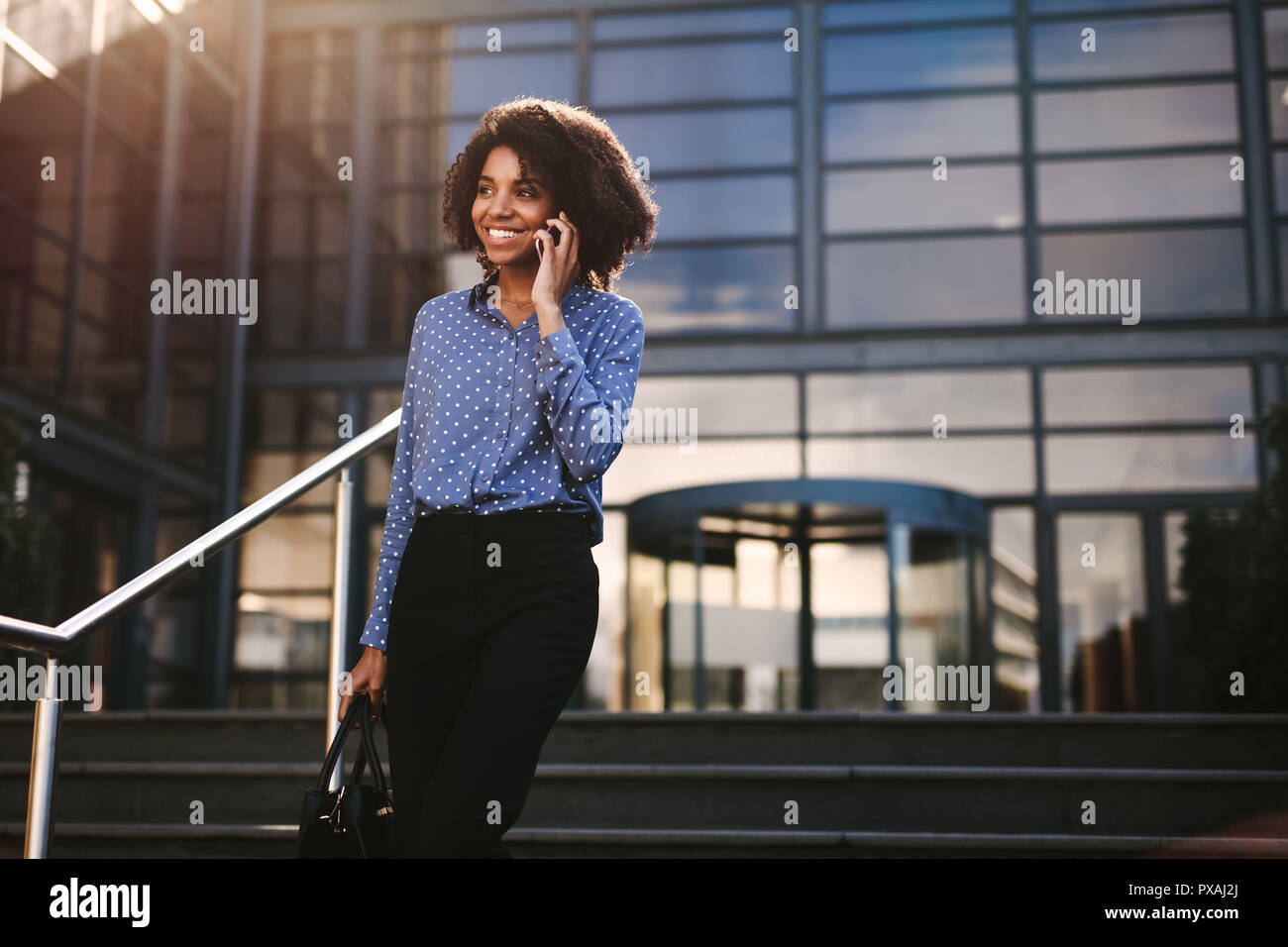 Woman walking down the steps outside office building and talking on ...