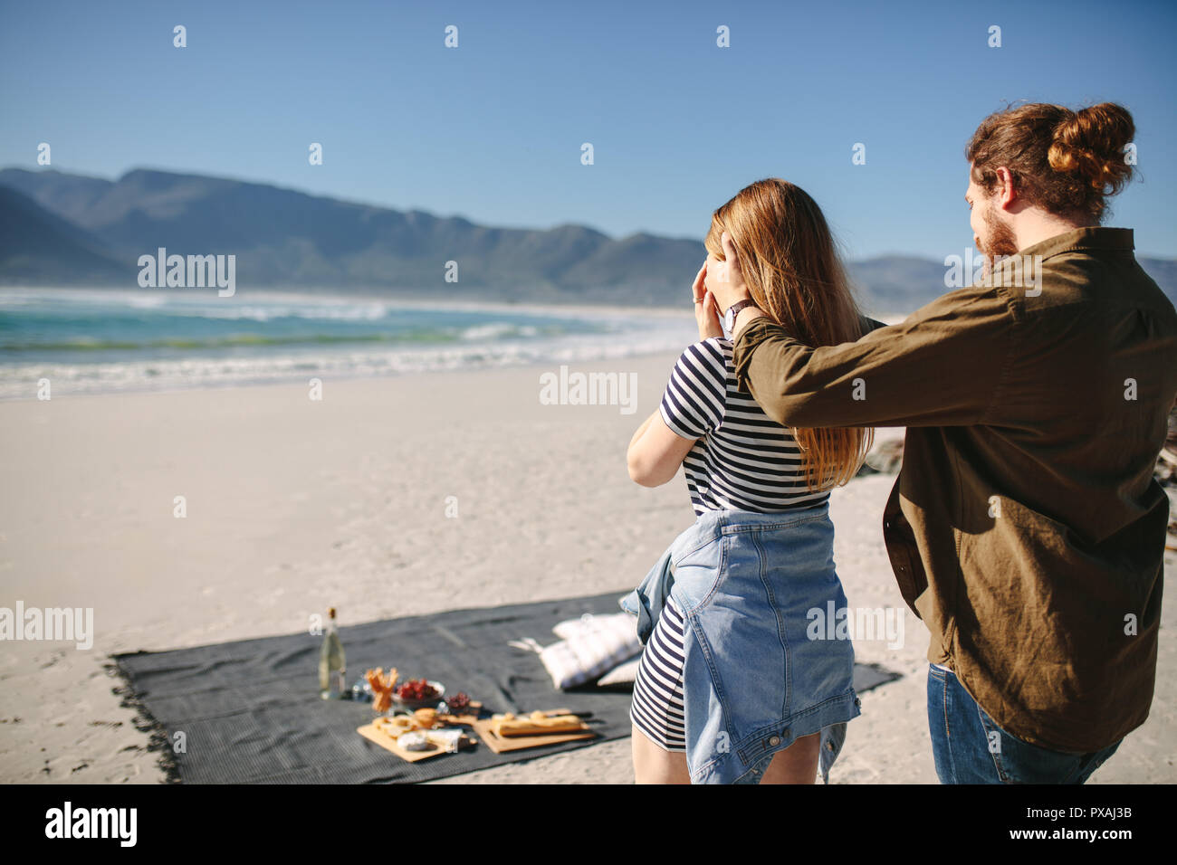 Rear view of man covering eyes of his girlfriend on beach to surprise ...
