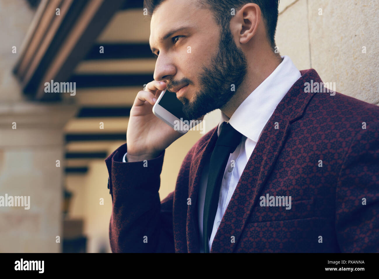 Handsome and fashionable man with a beard talking on the phone in close ...