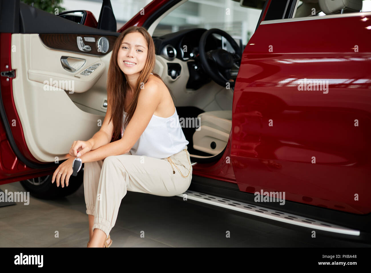 Smiling woman choosing new car at car showroom and reading properties ...