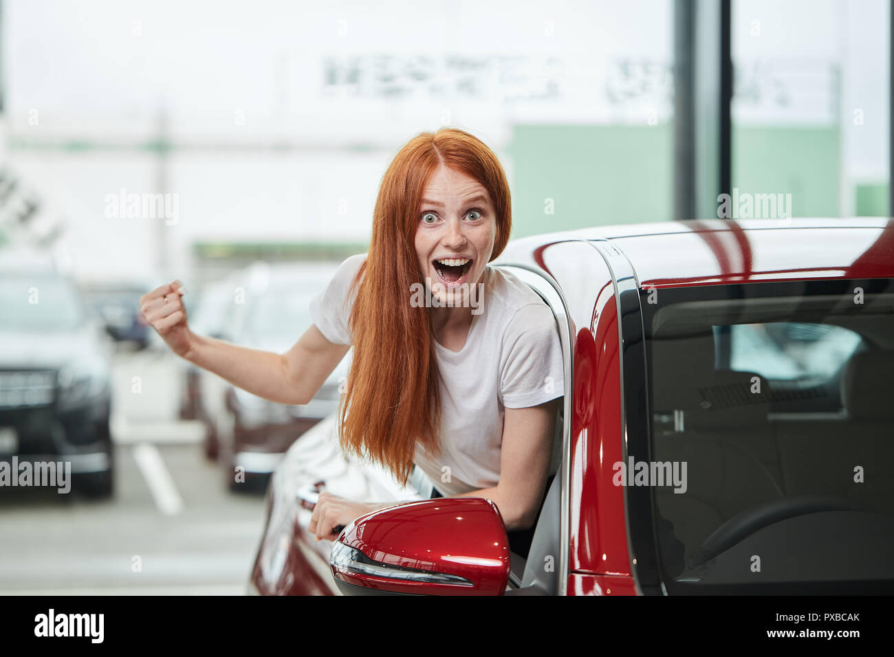 young happy woman surprised by a new car at car showroom, gift from her ...