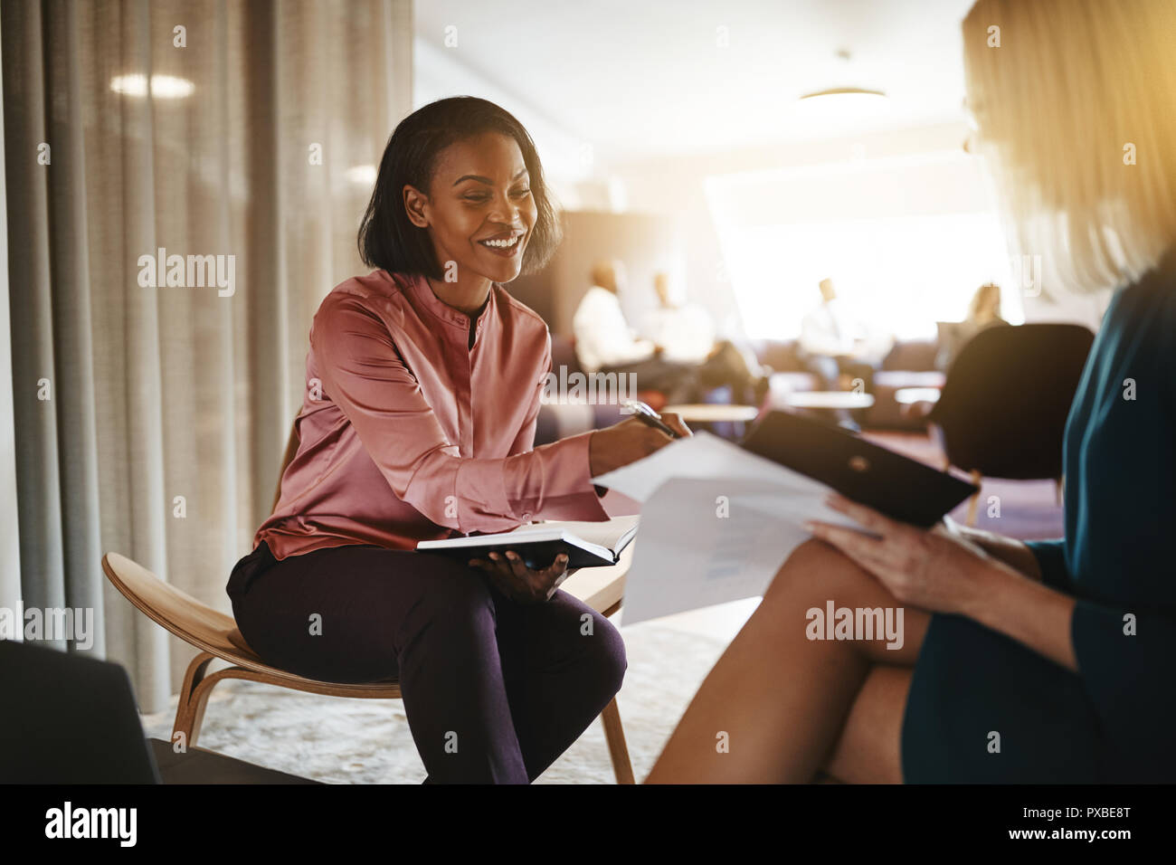 Smiling young businesswoman sitting with a coworker in a modern office ...