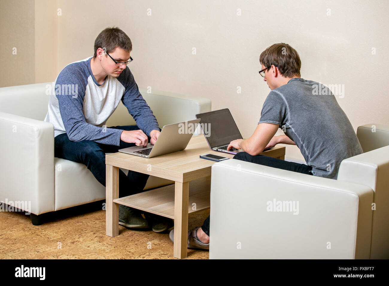 Two young people working on laptops in the office, writing a program ...
