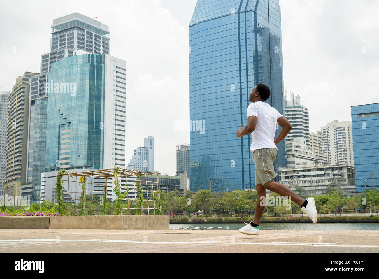 Young African man running outdoors in park with cityscape Stock Photo ...