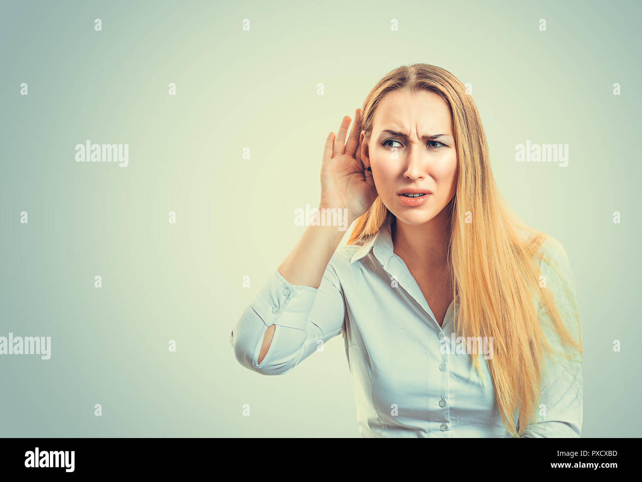 Blond woman in white shirt frowning while trying to listen to gossips ...