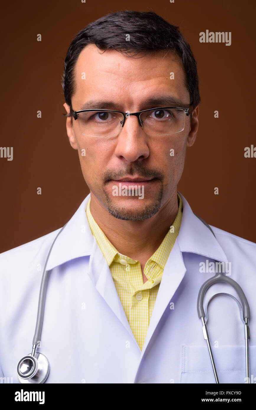 Portrait of handsome man doctor face against brown background Stock ...