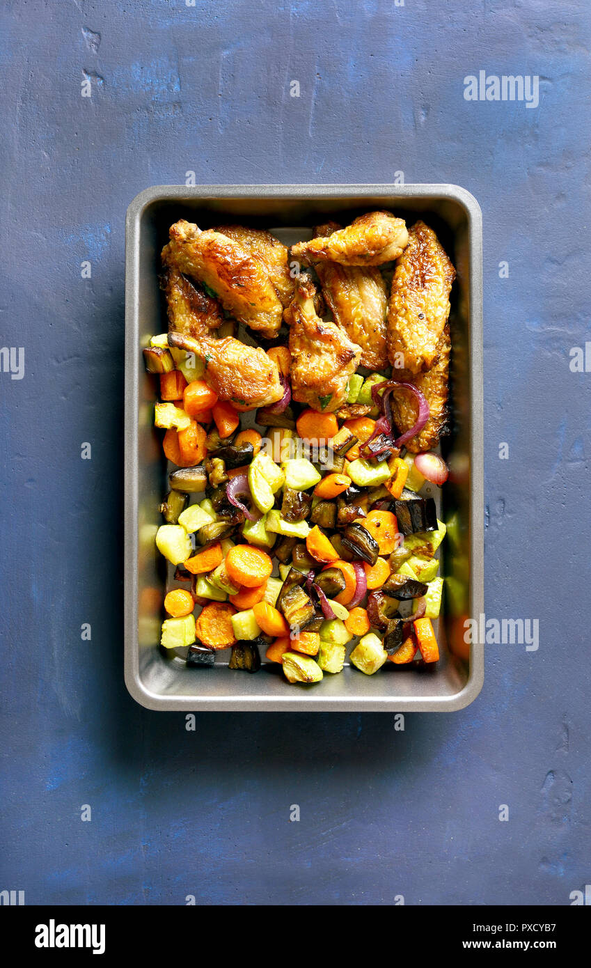 Grilled vegetables with chicken wings in baking tray on blue stone ...