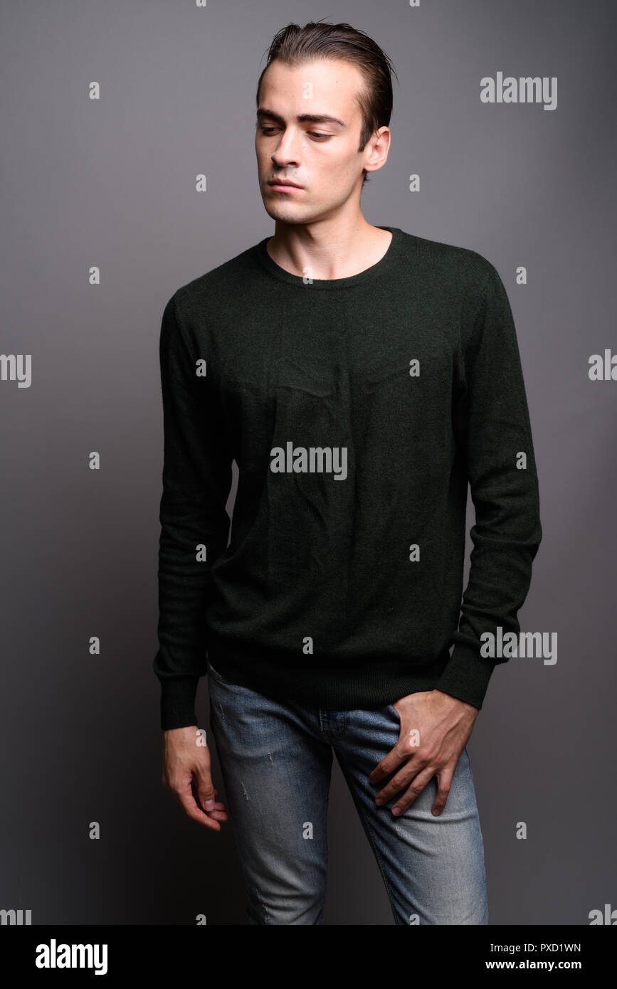 Young handsome man thinking and looking down against gray Stock Photo ...