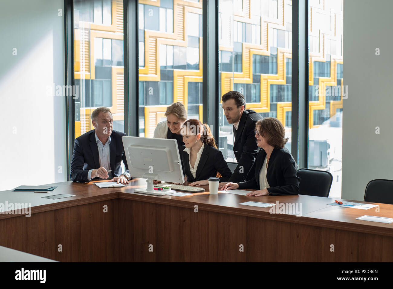 Business team look at one computer monitor having discussion in office ...