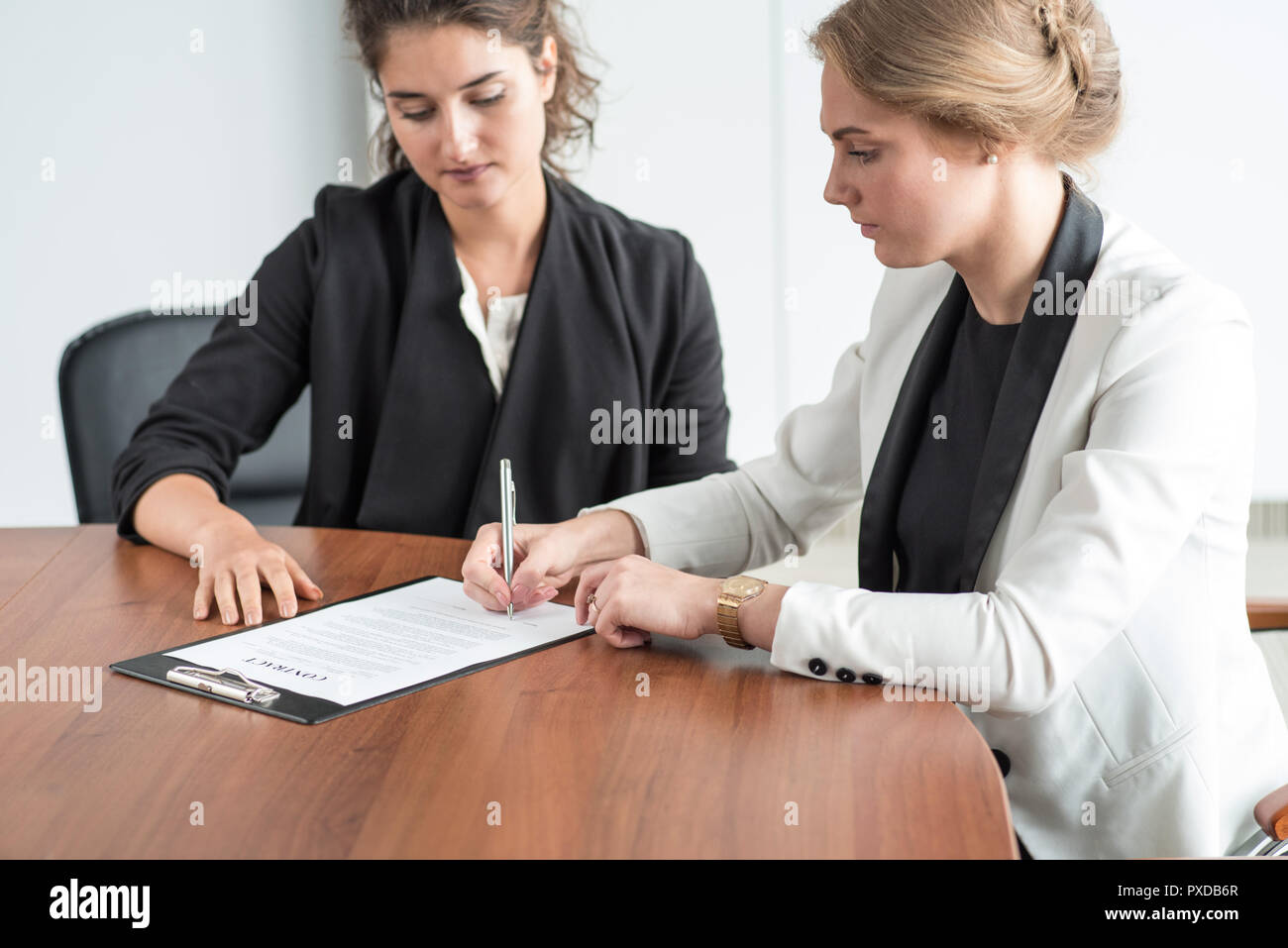 Two business women signing a document at conference table Stock Photo ...