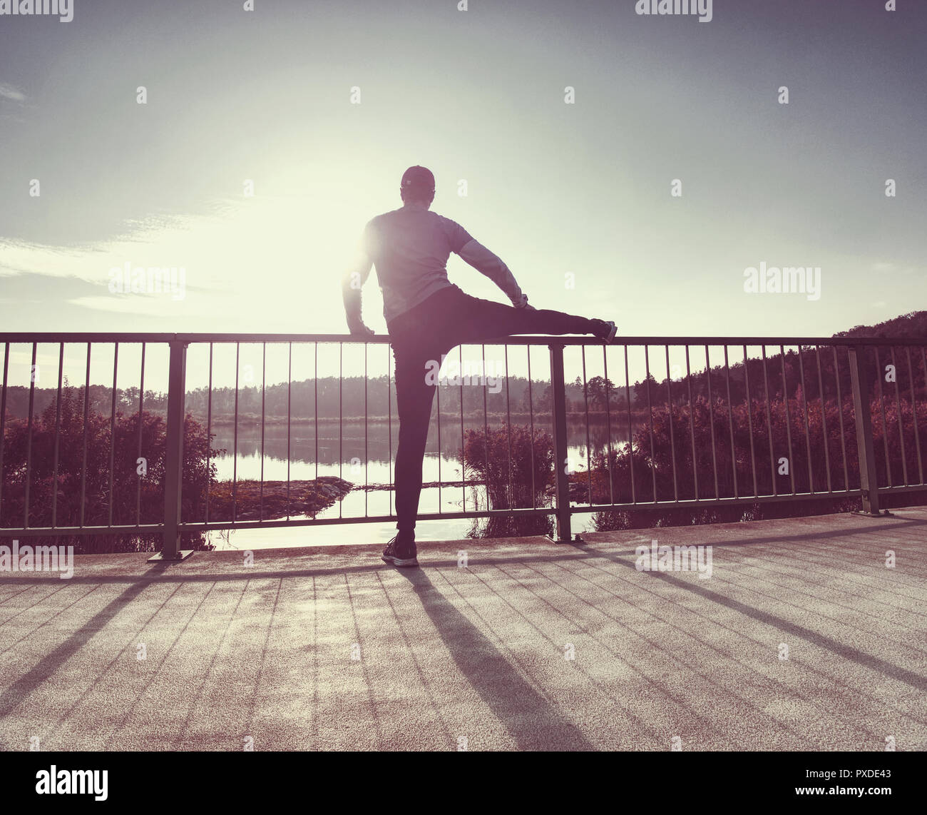 Tall sportsman warming up his muscles, stretching his legs before ...