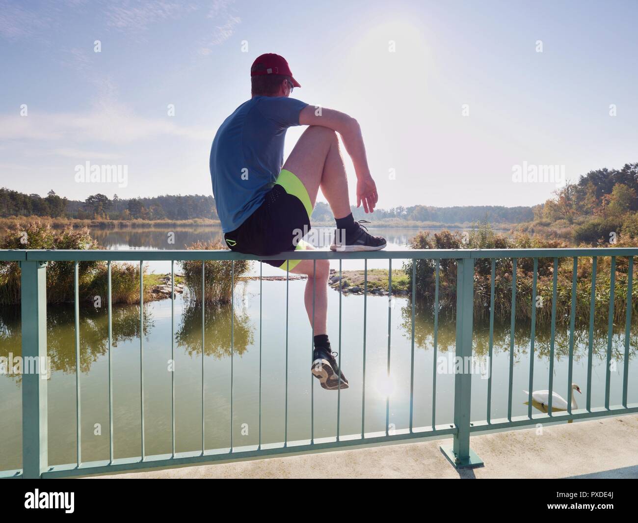 Sportsman is sitting on handrail with legs over bar in the park. Feet ...