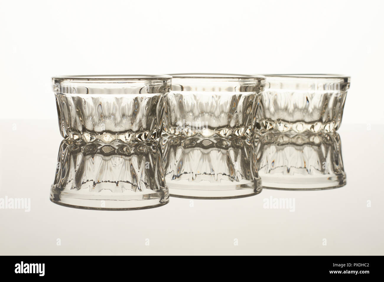 Three glass cups on reflective table Stock Photo - Alamy
