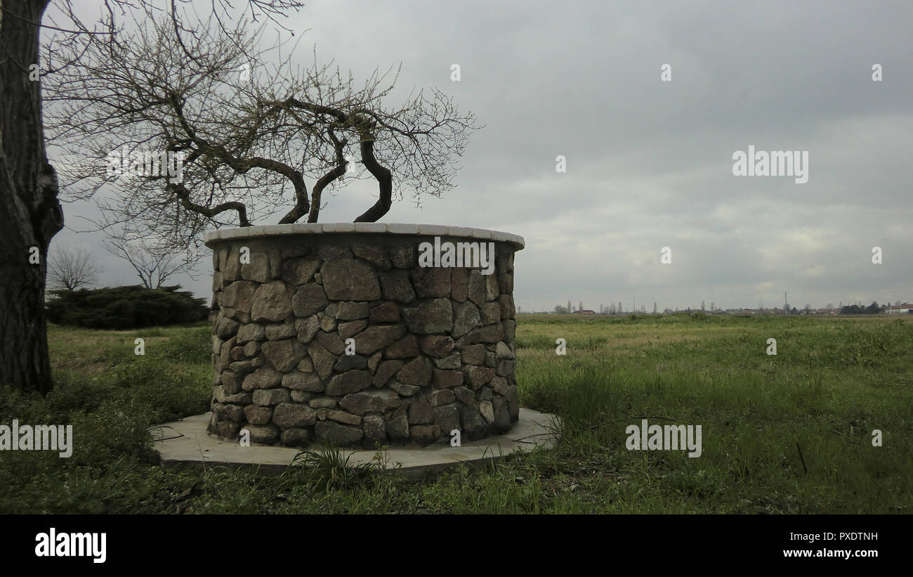 Panorama with a well made of stones in a rural landscape with cloudy ...