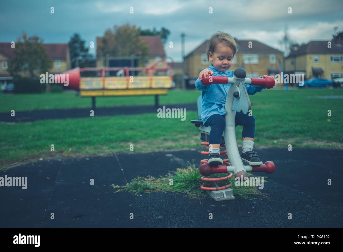A little toddler is sitting on the play equipment at a playground Stock ...