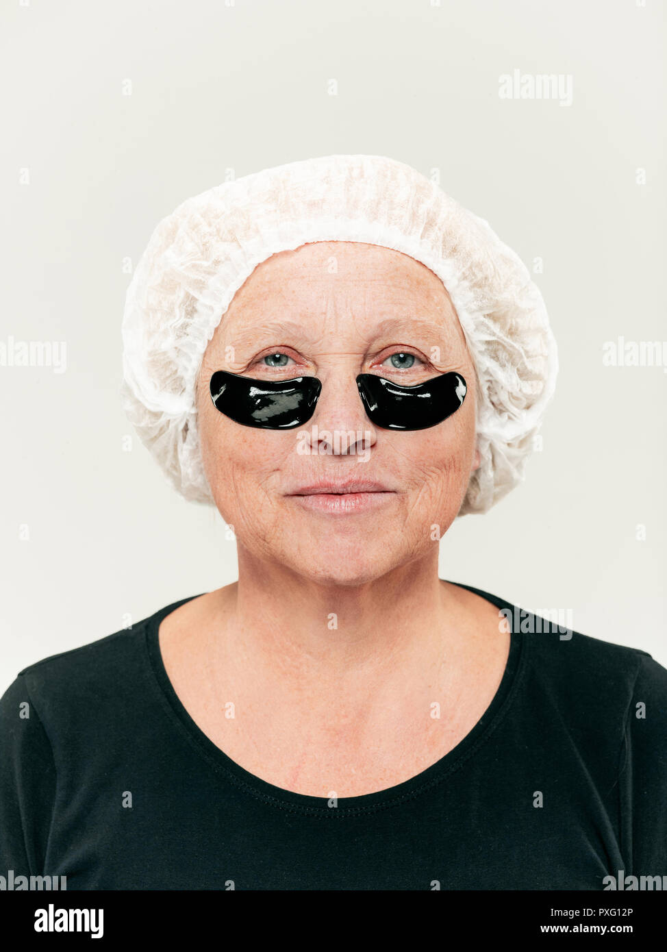 Senior woman isolated on white wall looking at camera making masks ...