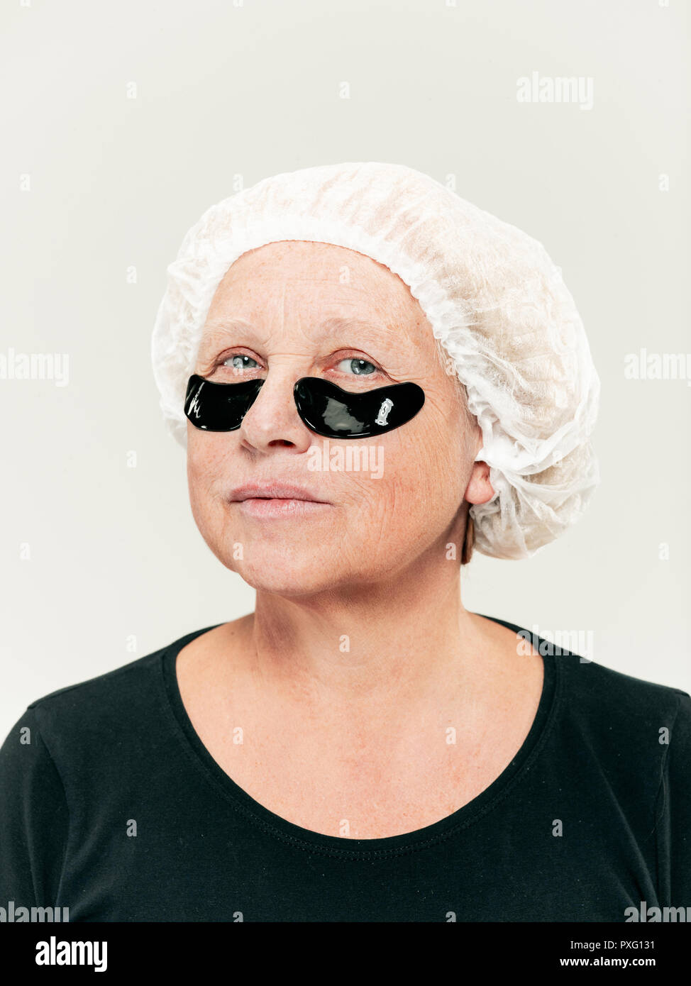 Senior woman isolated on white wall looking at camera making masks ...