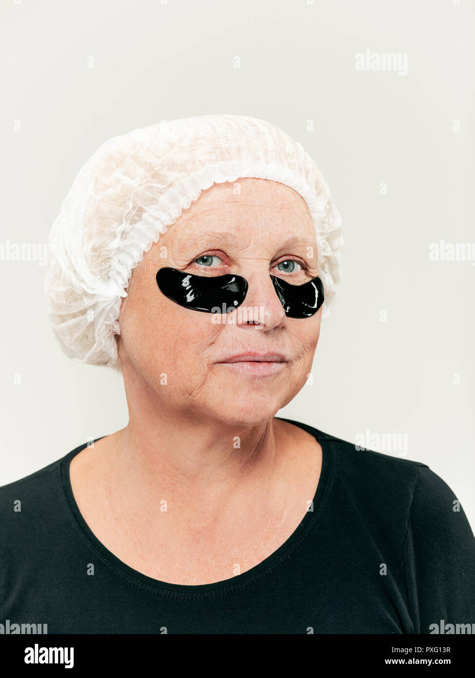 Senior woman isolated on white wall looking at camera making masks ...