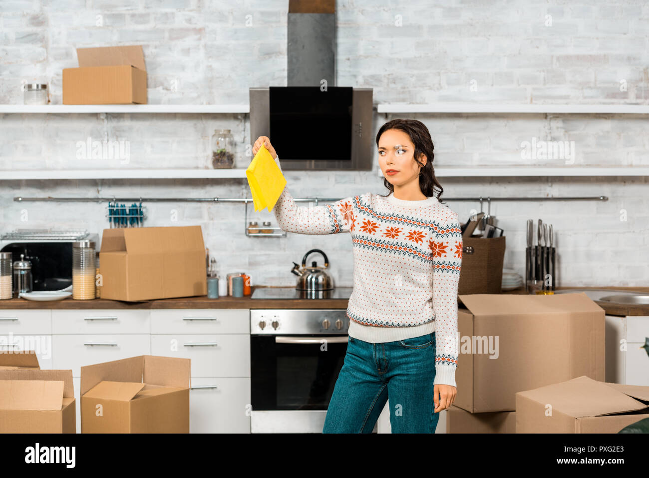 young woman holding dirty yellow rag in kitchen with cardboard boxes at ...