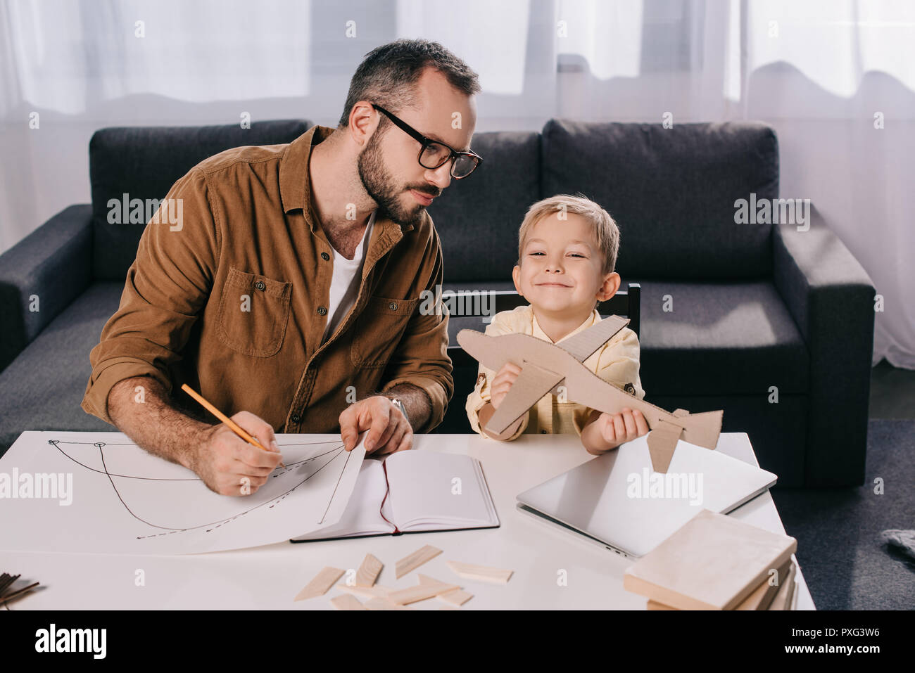 father in eyeglasses and cute little son modeling plane together at ...