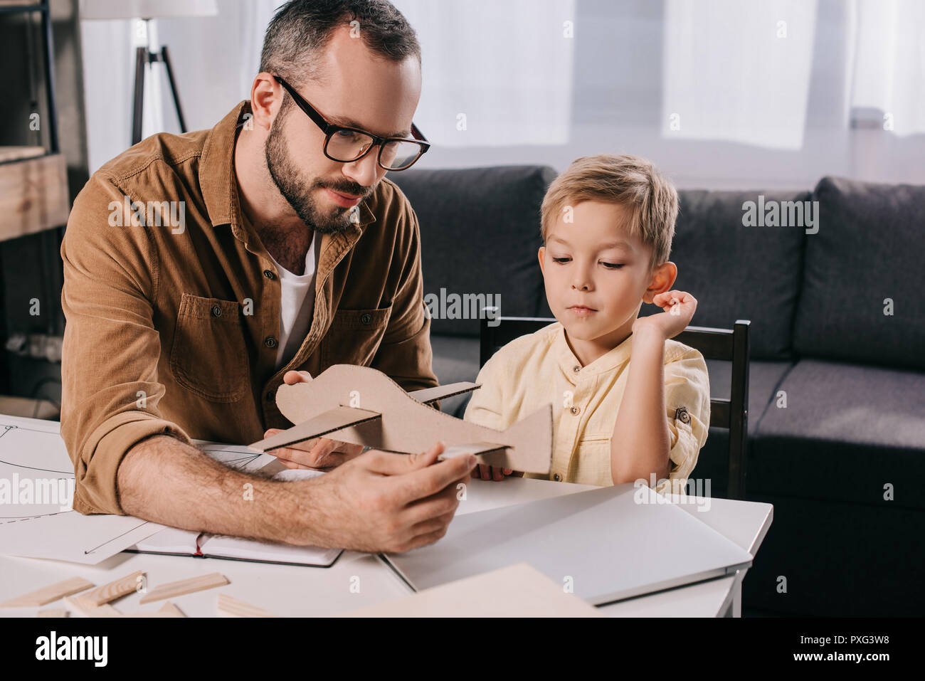 father in eyeglasses and cute little son modeling plane together at ...