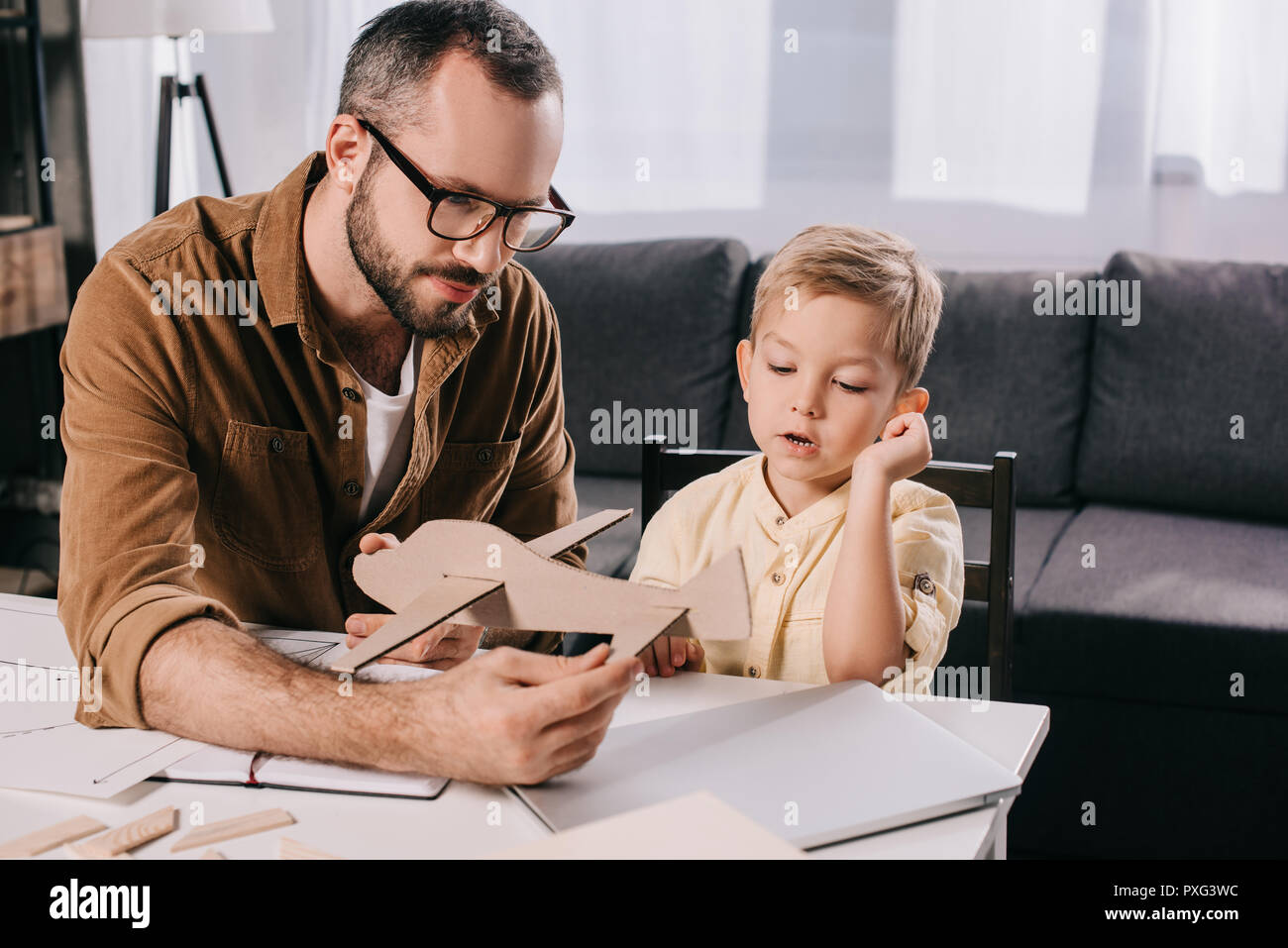 father in eyeglasses and adorable little boy modeling wooden plane ...