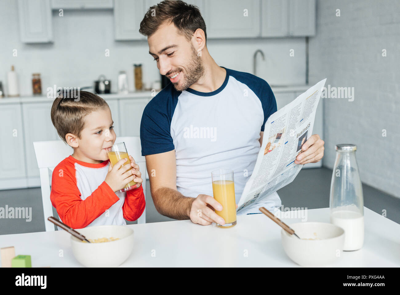 father with newspaper looking at son drinking juice during breakfast in ...