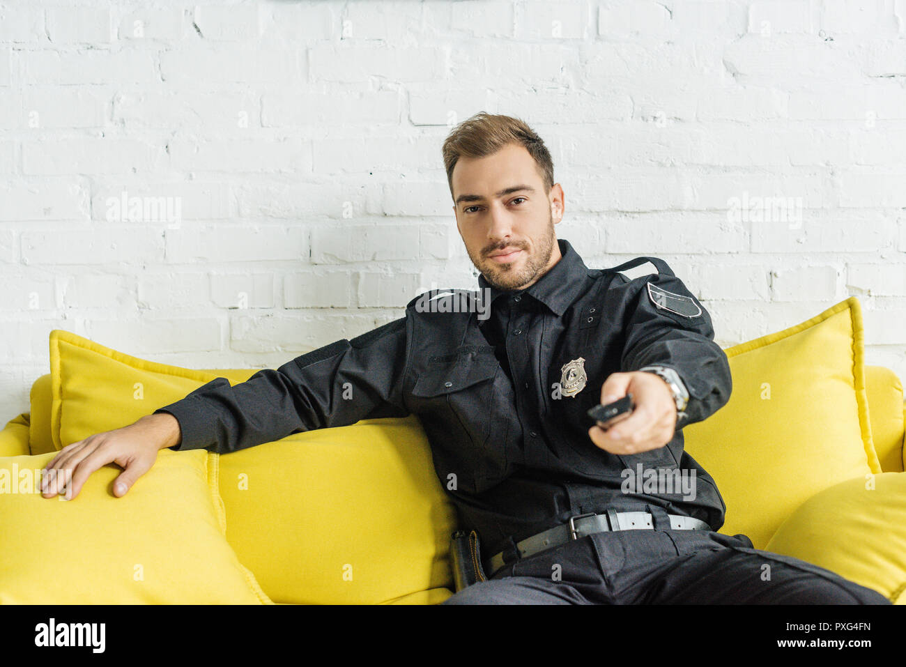 handsome young policeman sitting on couch and using tv remote control ...