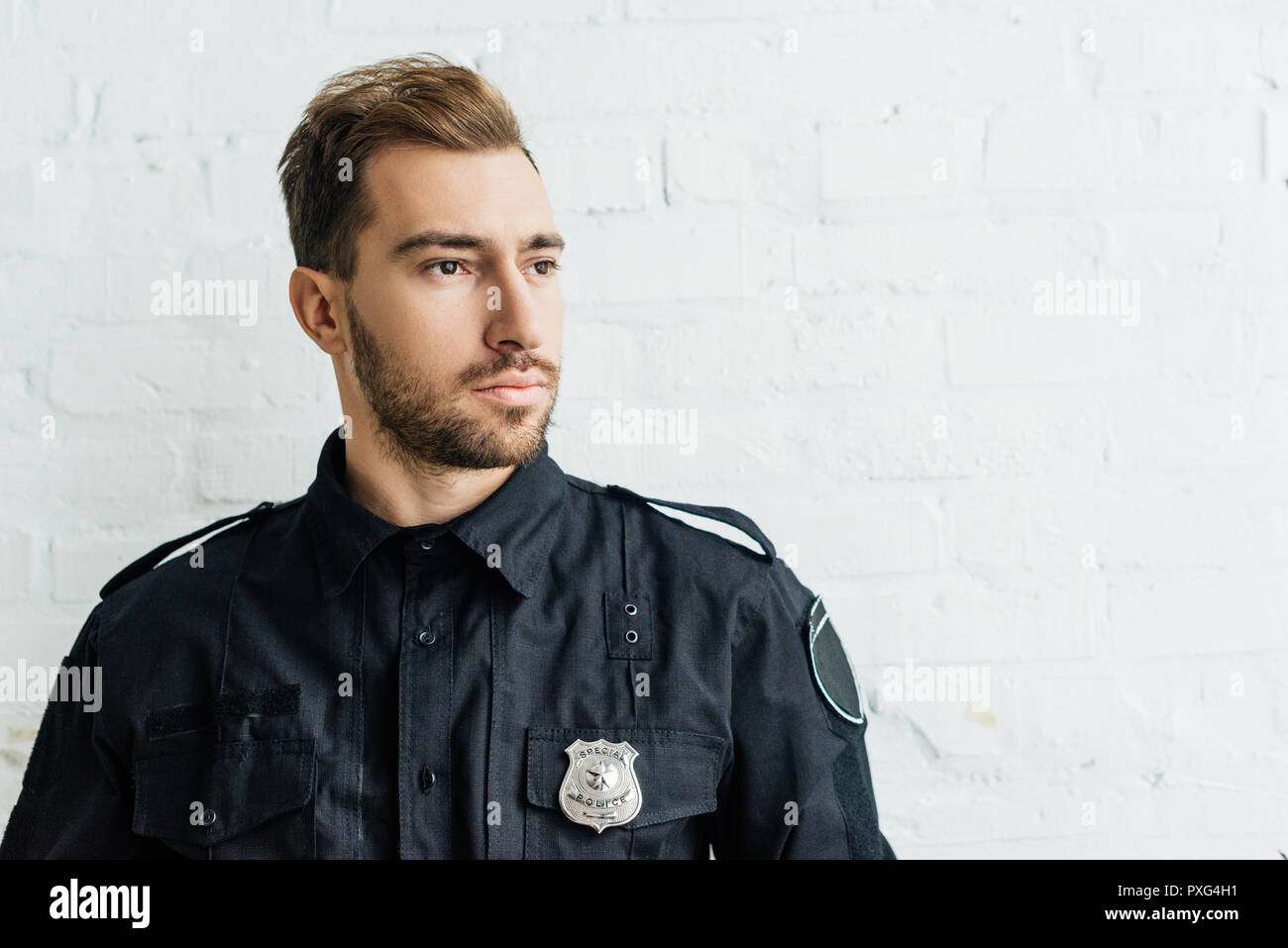 portrait of thoughtful young policeman in front of white brick wall ...