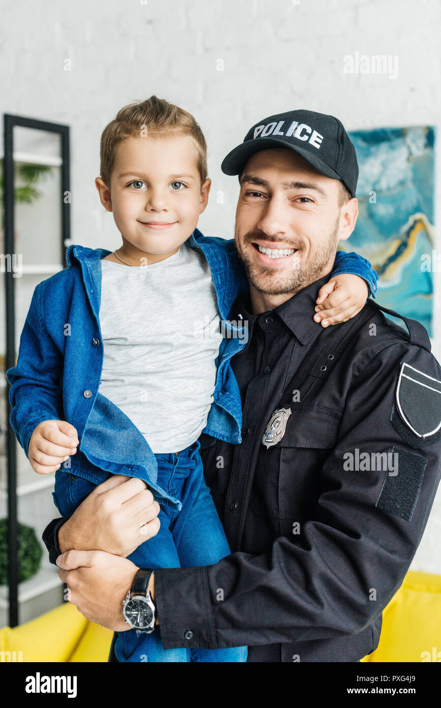 smiling young father in police uniform carrying his little son and ...