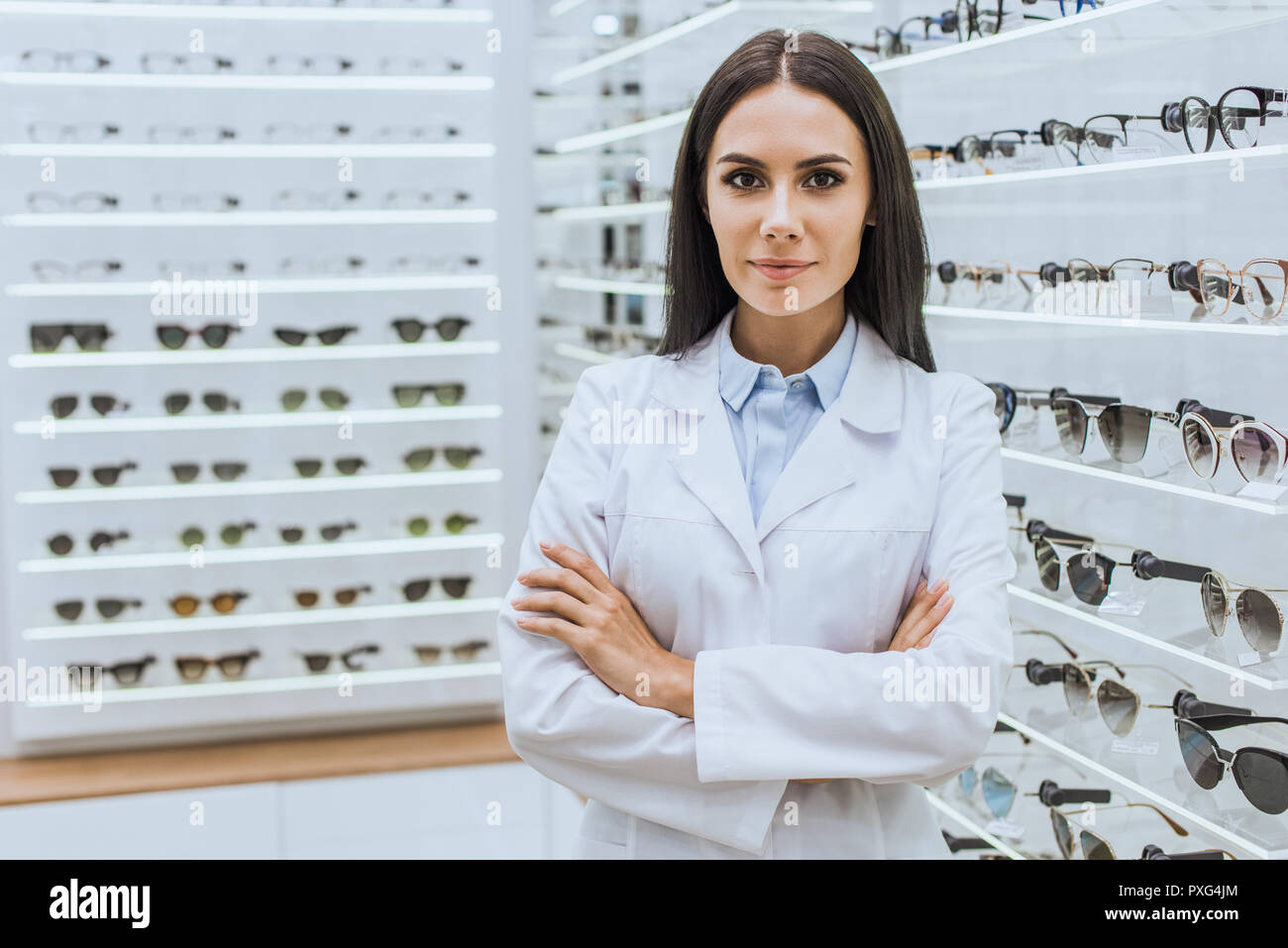 professional optometrist with crossed arms posing near shelves with ...