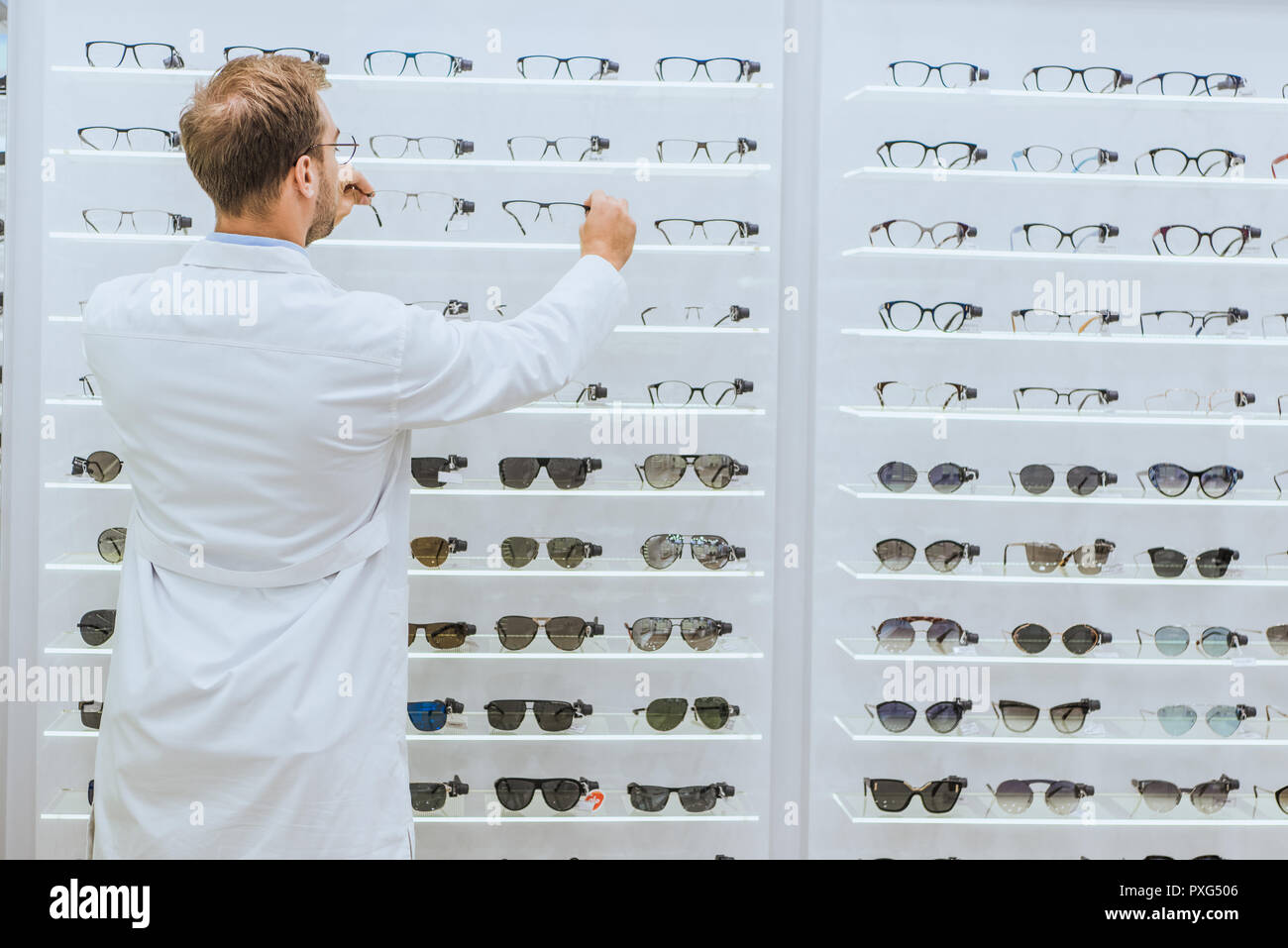back view of oculist in white coat taking glasses from shelves in ...