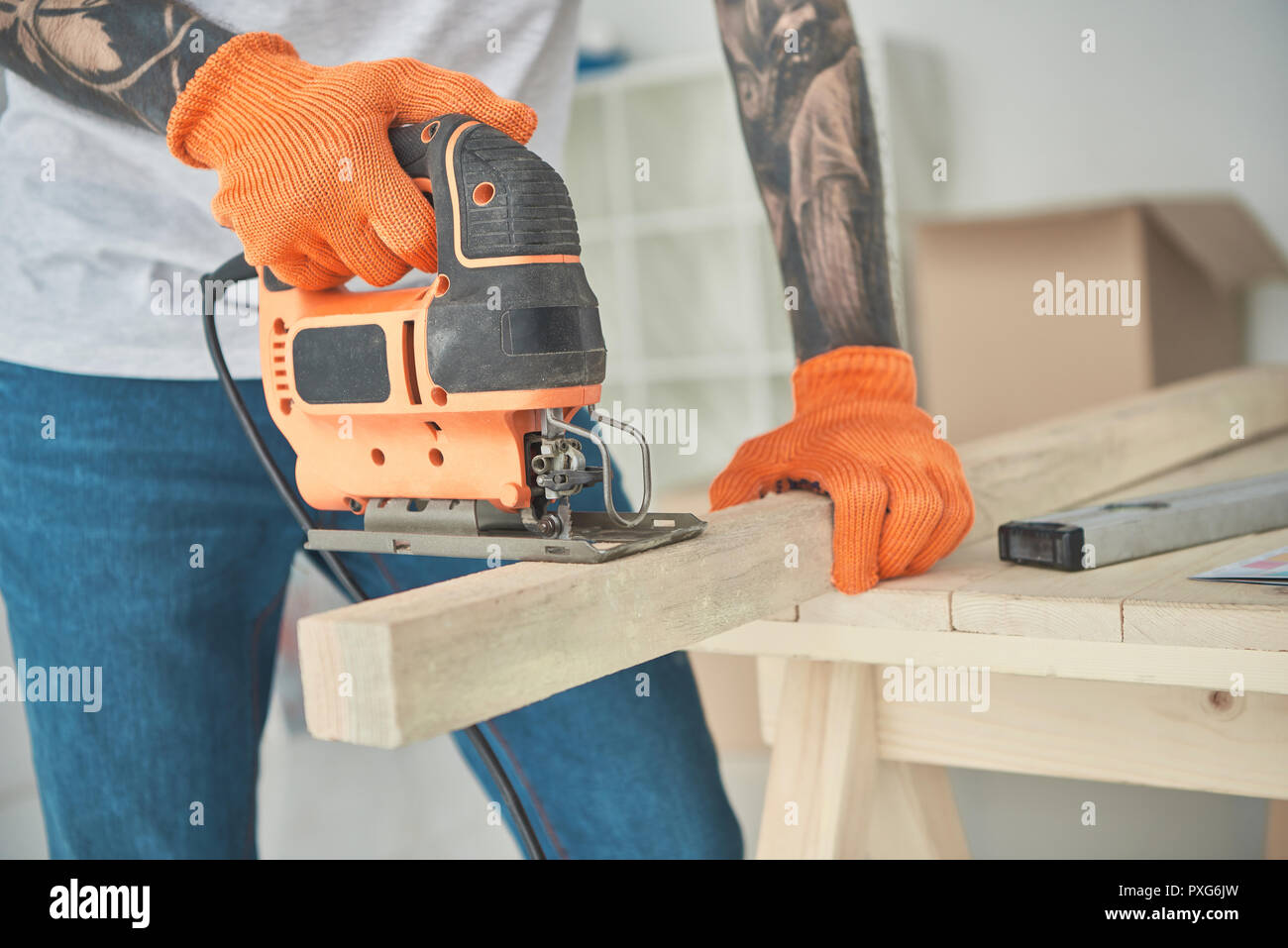 close-up partial view of of young tattooed man using electric jigsaw ...