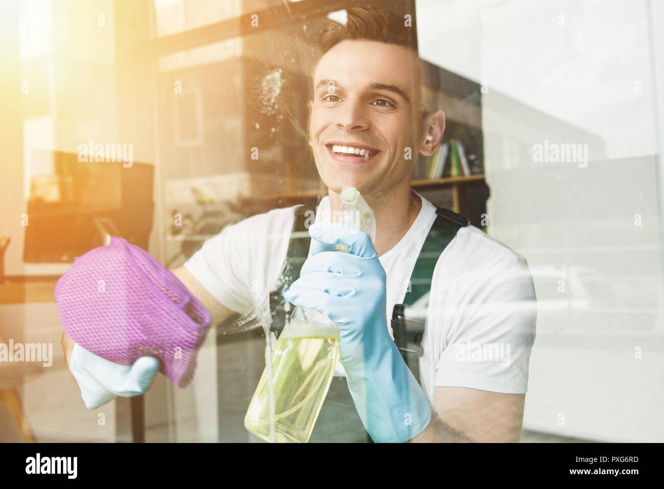 handsome smiling young man cleaning and wiping window with spray bottle ...