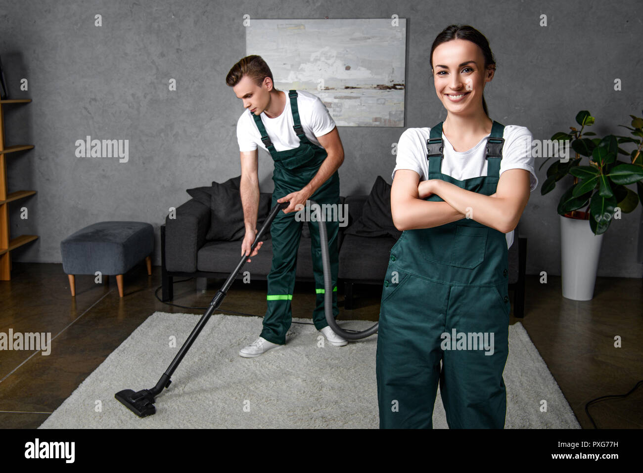young male cleaner using vacuum cleaner and female coworker standing ...